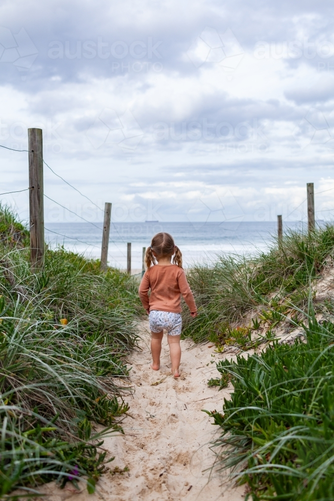 Image of Little girl standing on sandy beach track looking towards ...