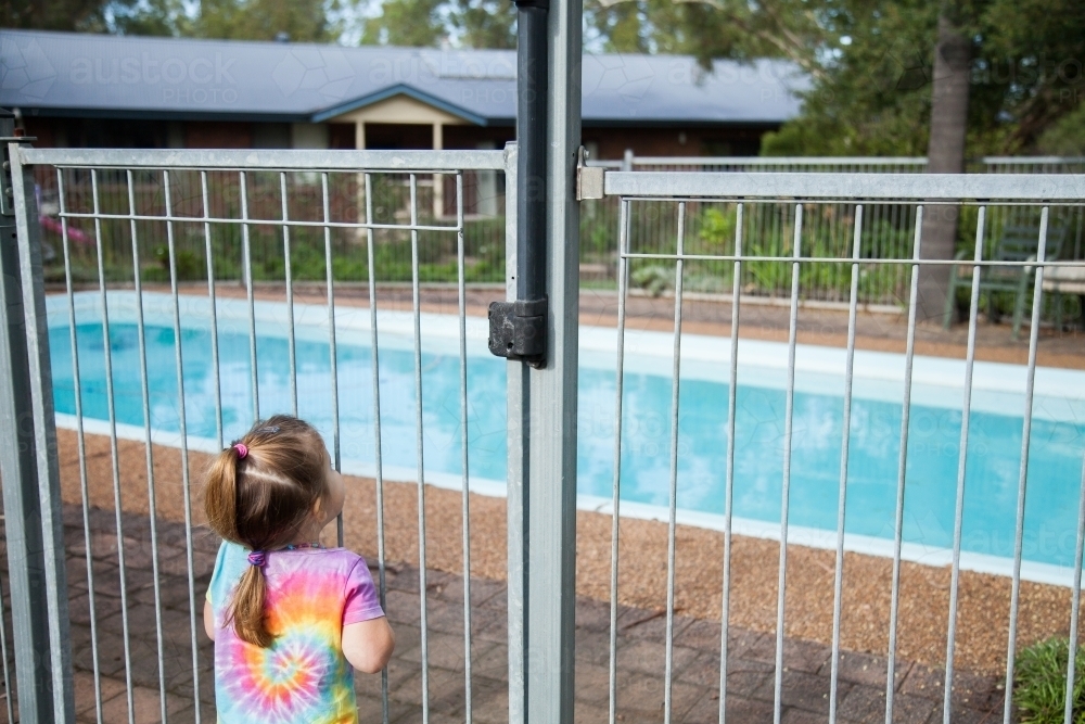 Image of Little girl standing safely outside pool fence gate looking in ...