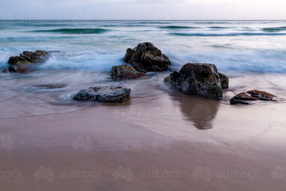 Image of Long exposure of ocean and boulders on beach at dawn ...