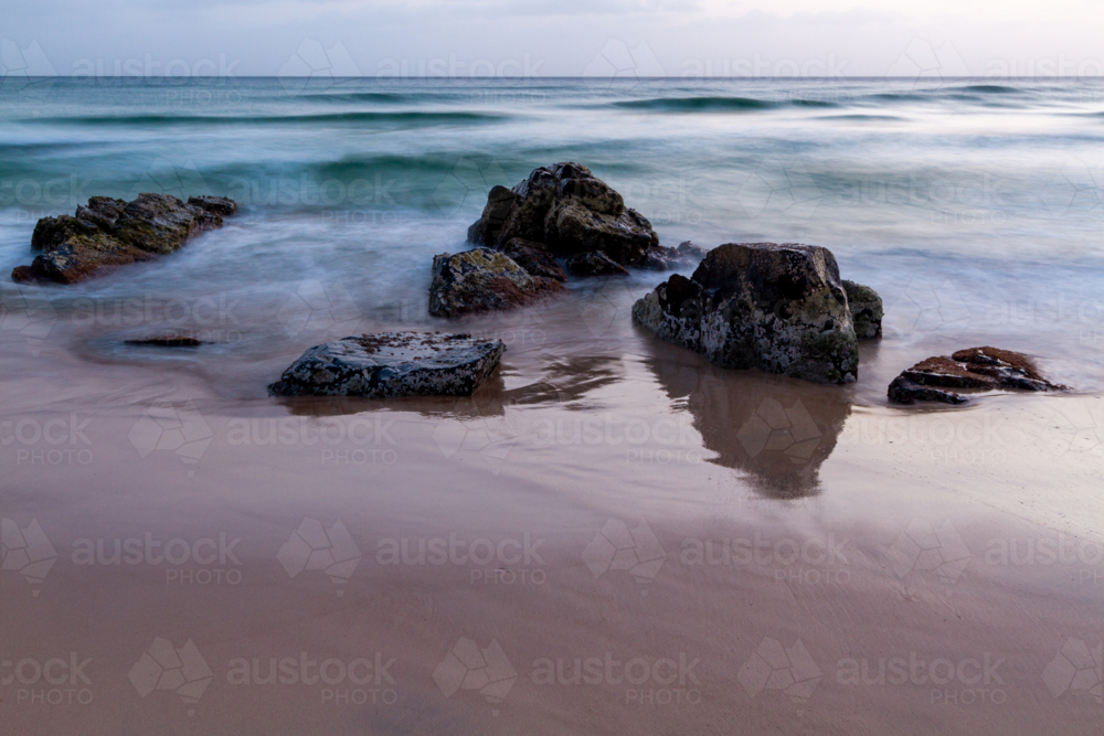 Image of Long exposure of ocean and boulders on beach at dawn ...