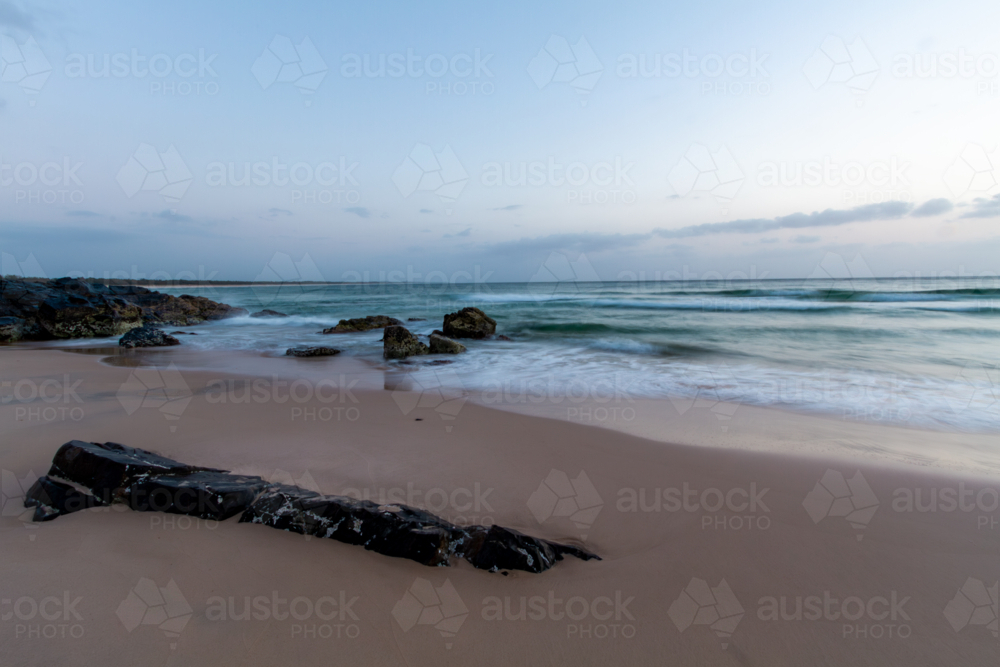 Image of Long exposure of the ocean and boulders on beach at dawn ...