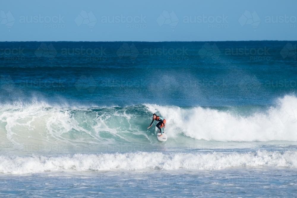 Image of Long shot of female surfer catching an empty wave - Austockphoto