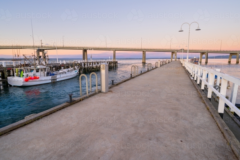 Image of Looking along a wide concrete jetty with fishing boat docked ...