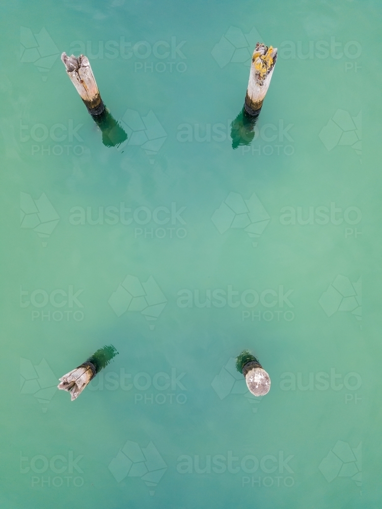 Image of Looking down on a row of old jetty pylons in turquoise water ...