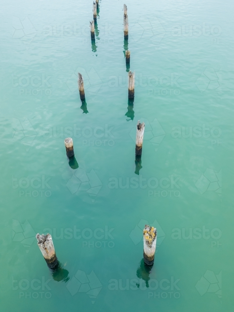 Image of Looking down on a row of old jetty pylons in turquoise water ...