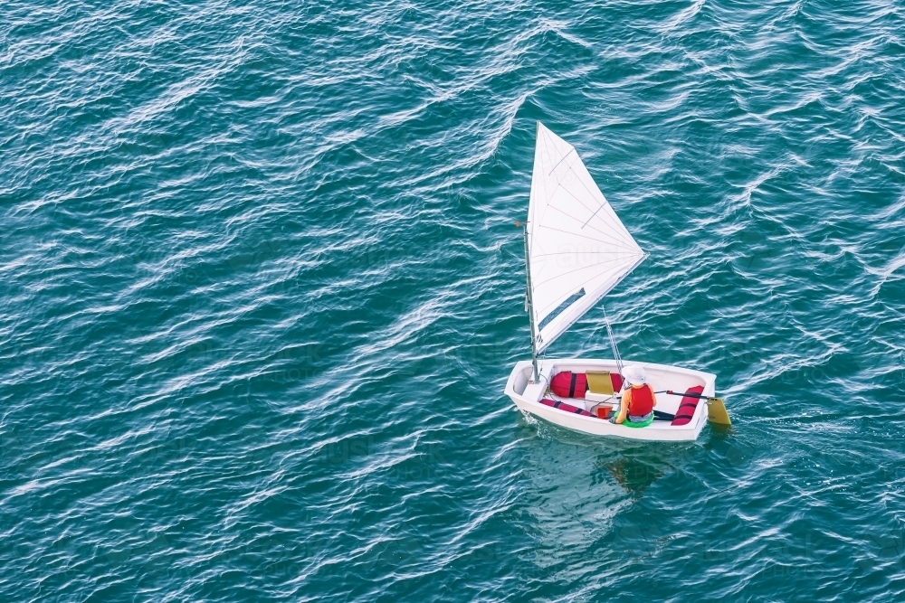 Image of Looking down on a sailor in a small boat on a blue sea ...