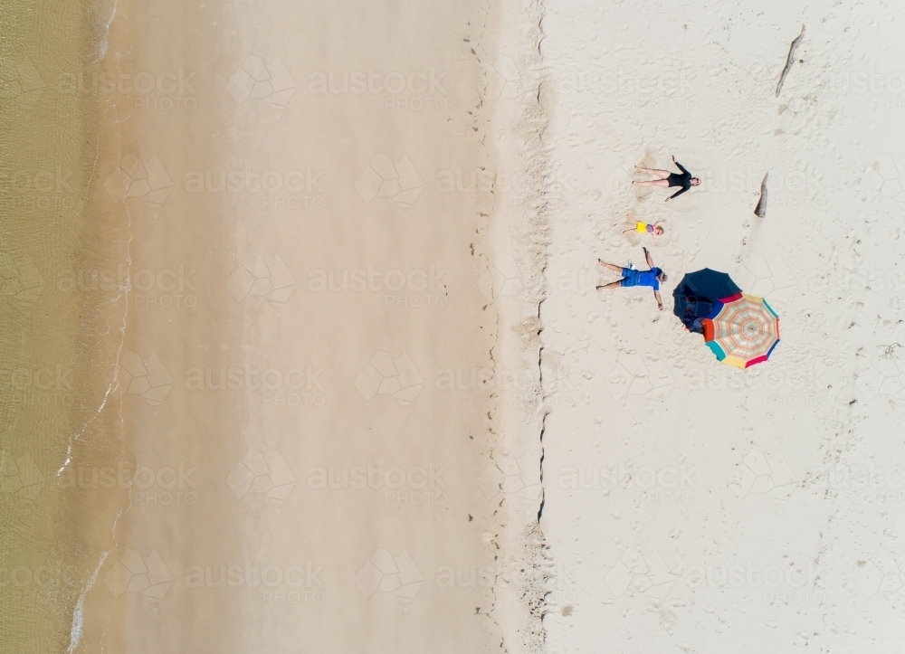 Image of Looking down on family making sand angels on a beach ...