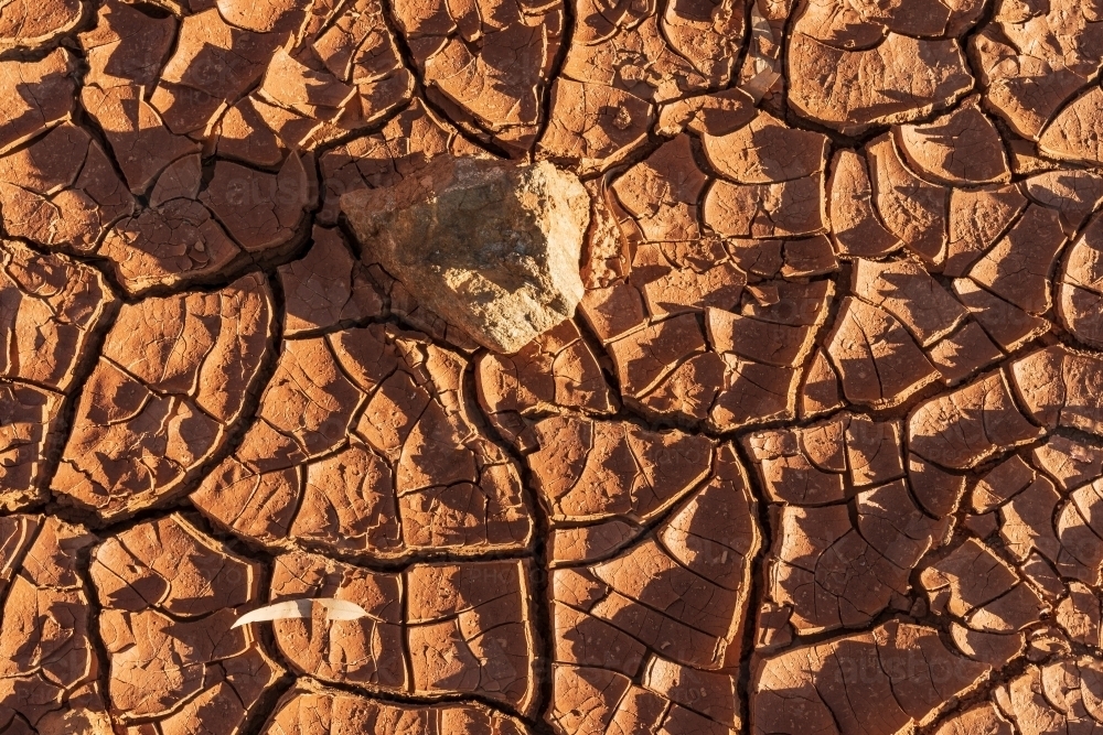 Image of Looking straight down onto dry cracked red mud with a rock ...