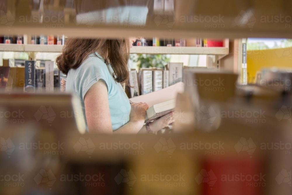 Image of Looking through shelves at a teen girl choosing a book to ...