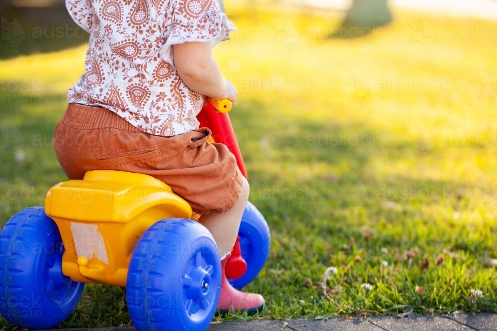 Image of Lower body shot of toddler riding tricycle on lawn grass ...