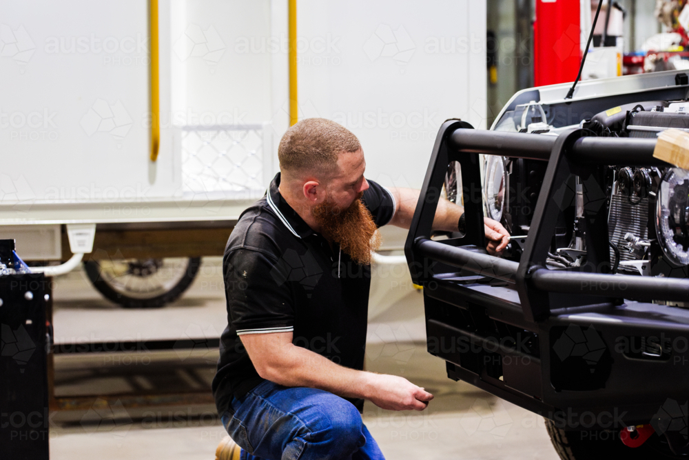 Image of Male Aussie mechanic kneeling on the floor working on front ...