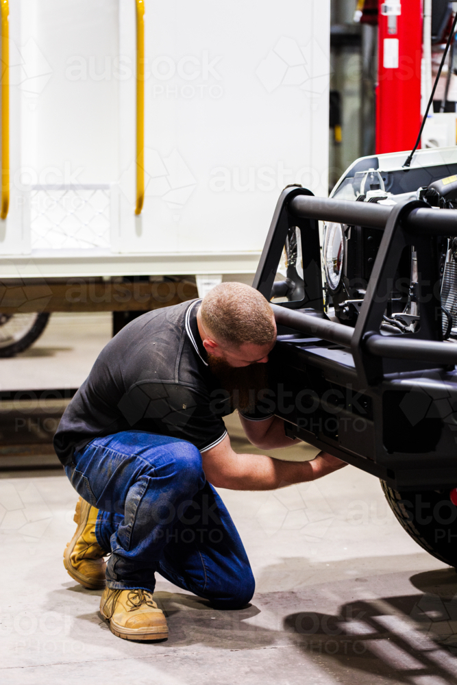 Image of Male Aussie mechanic kneeling on the floor working on front ...