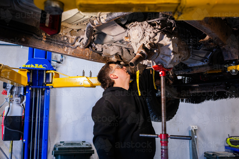 Image of Male mechanic working under vehicle raised on a hydraulic lift ...