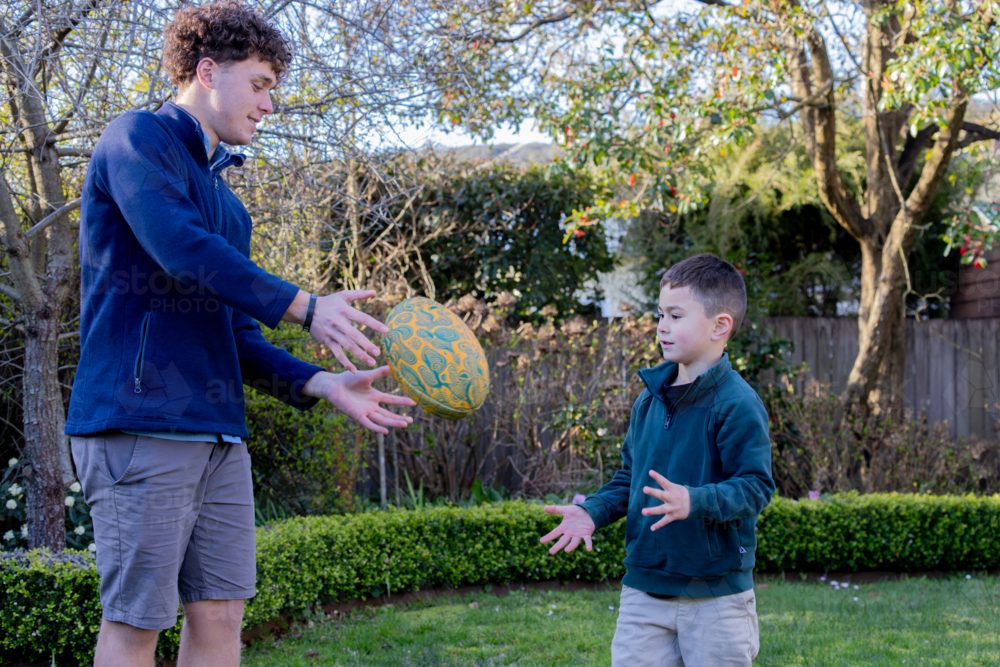 Image of Male siblings passing the footy to each other in the backyard ...