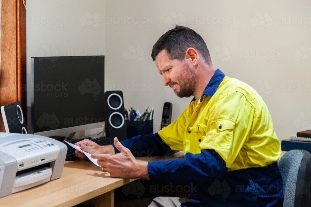 Image of Male tradie in his 30's sitting at his computer stressed out ...