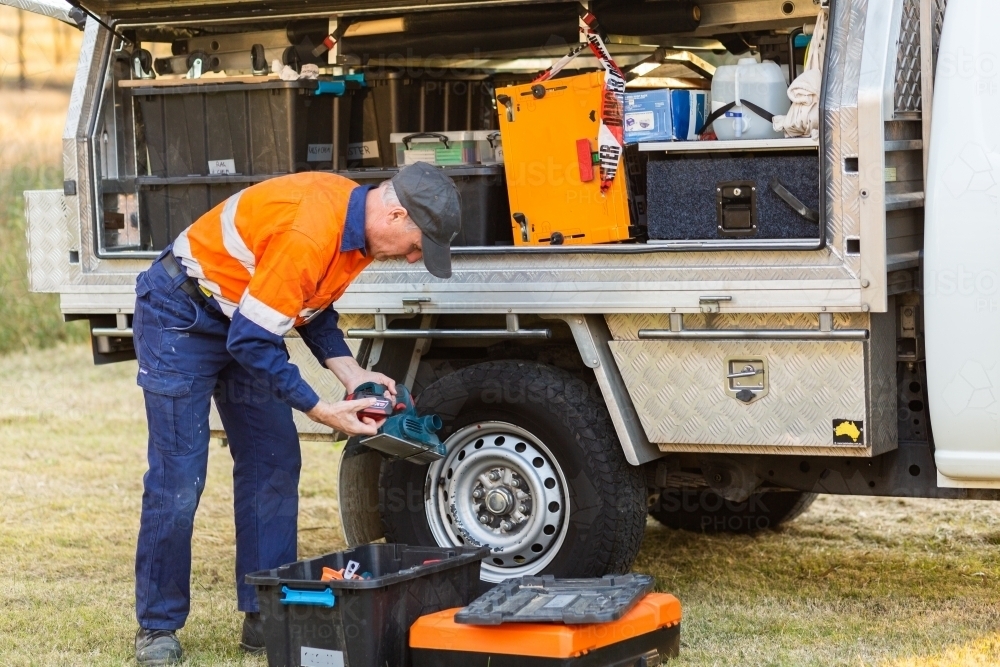 Image of male tradie opening box of tools beside ute - Austockphoto