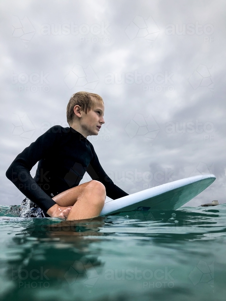 Image of Male youth sitting on boogie board waiting for waves on ...