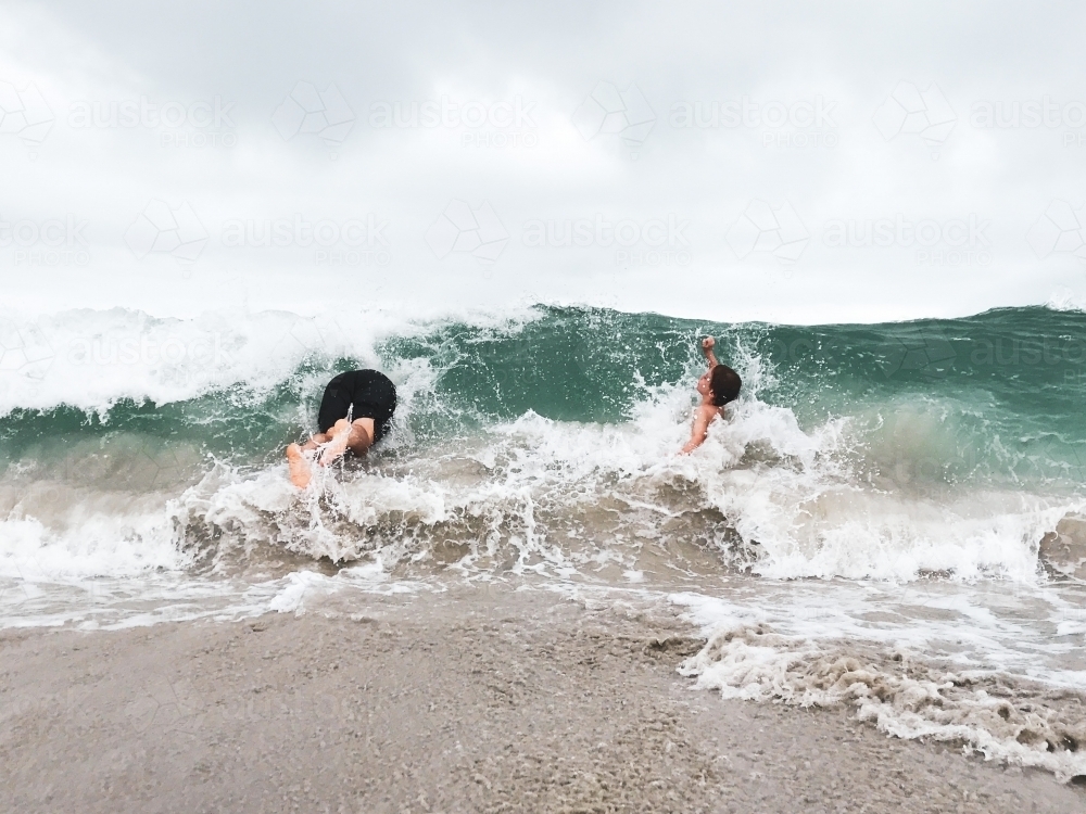 Image of Man and boy diving into waves at the beach - Austockphoto