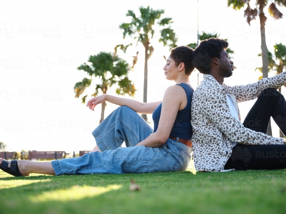 Image of Man and woman sitting back-to back in park - Austockphoto