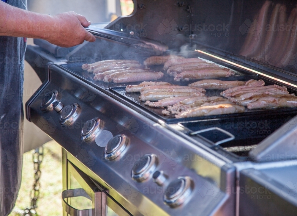 Image of Man cooking snags for dinner on a BBQ - Austockphoto