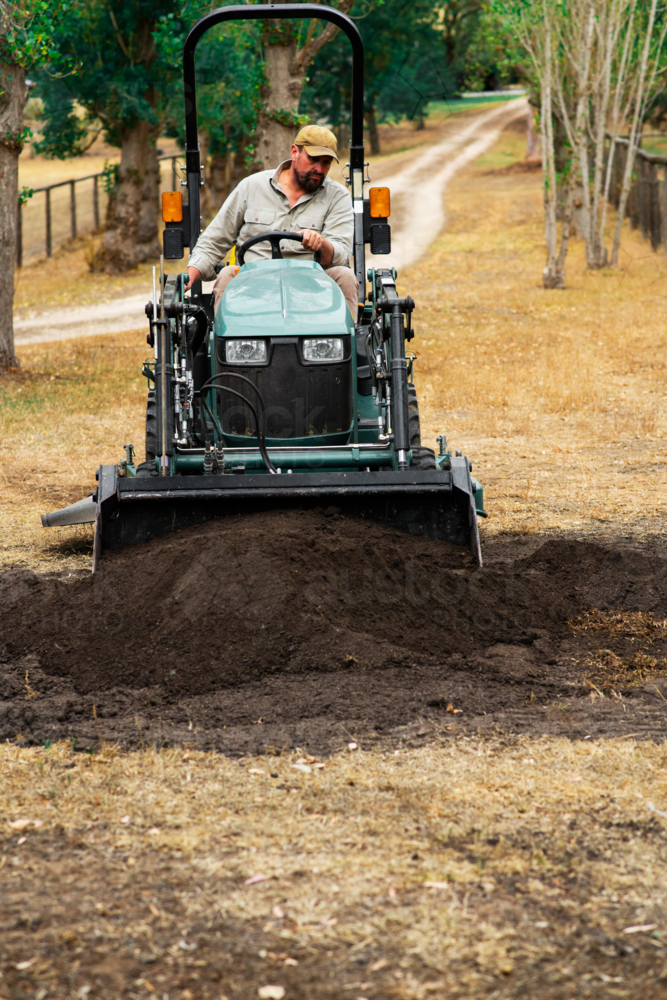 Image of man doing landscaping work on a small tractor - Austockphoto