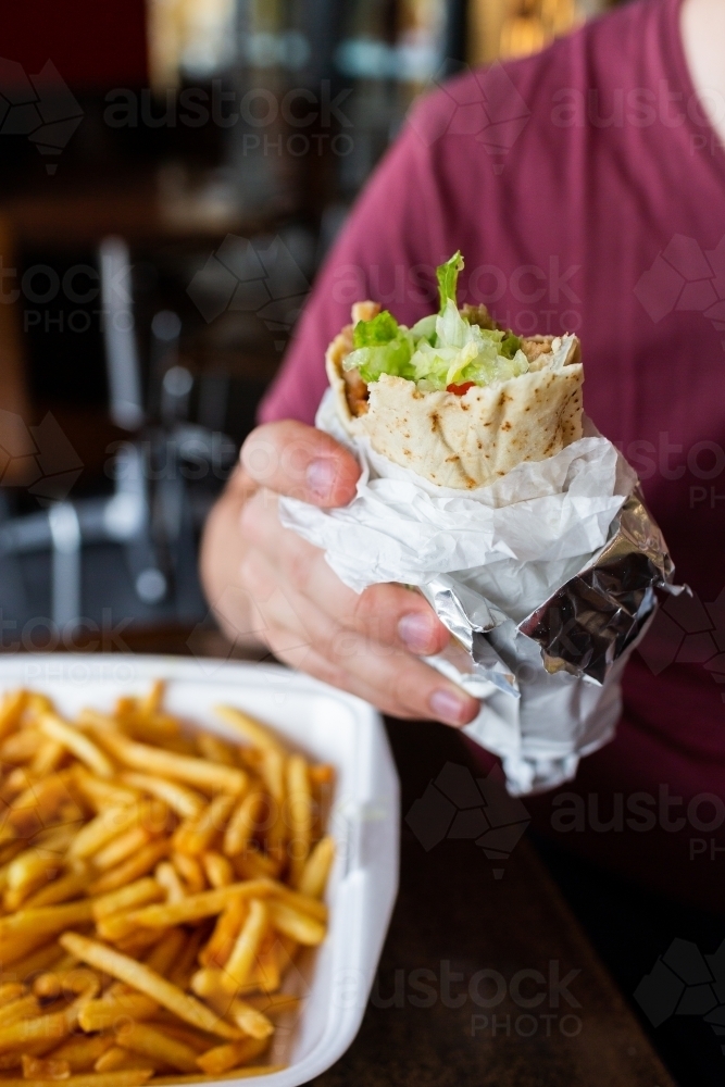 Image of Man eating a kebab wrap for lunch with chips - Austockphoto