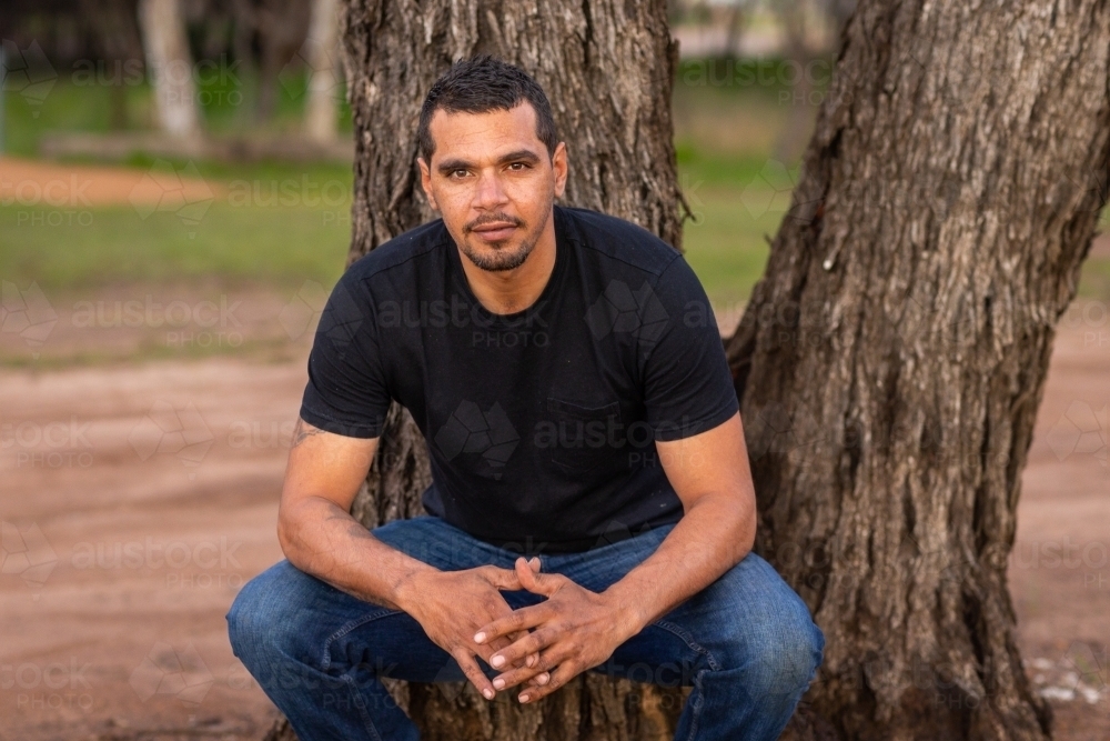 Image of man outdoors squatting in front of tree - Austockphoto
