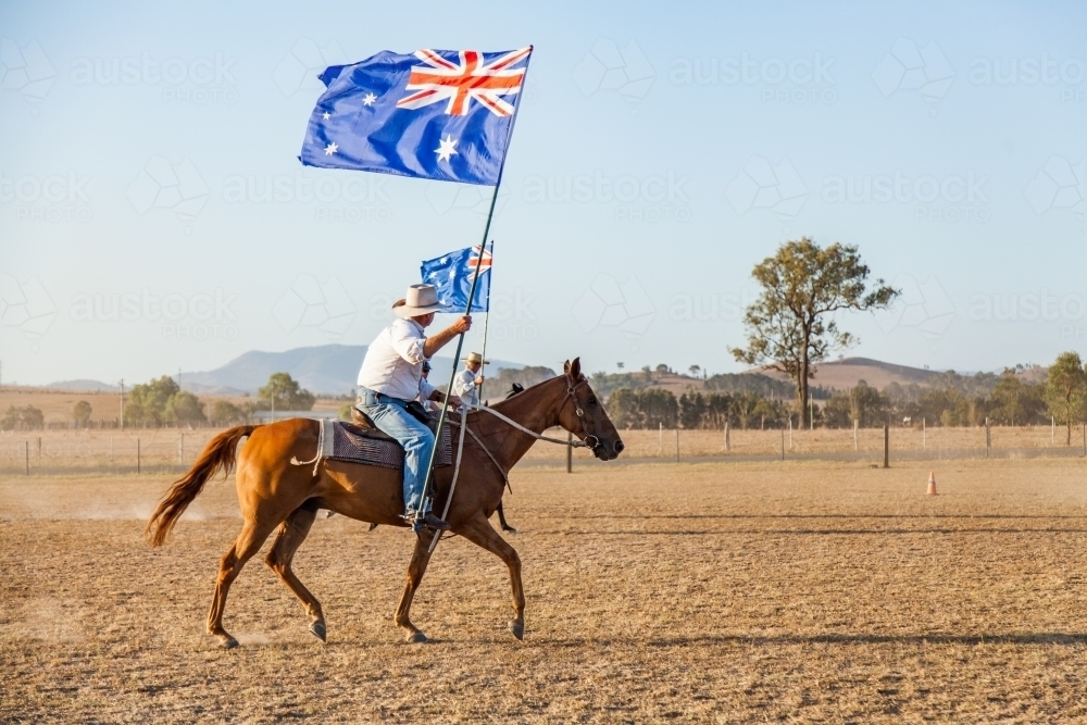 Image of Man riding Australian stock horse with flag in dusty paddock ...