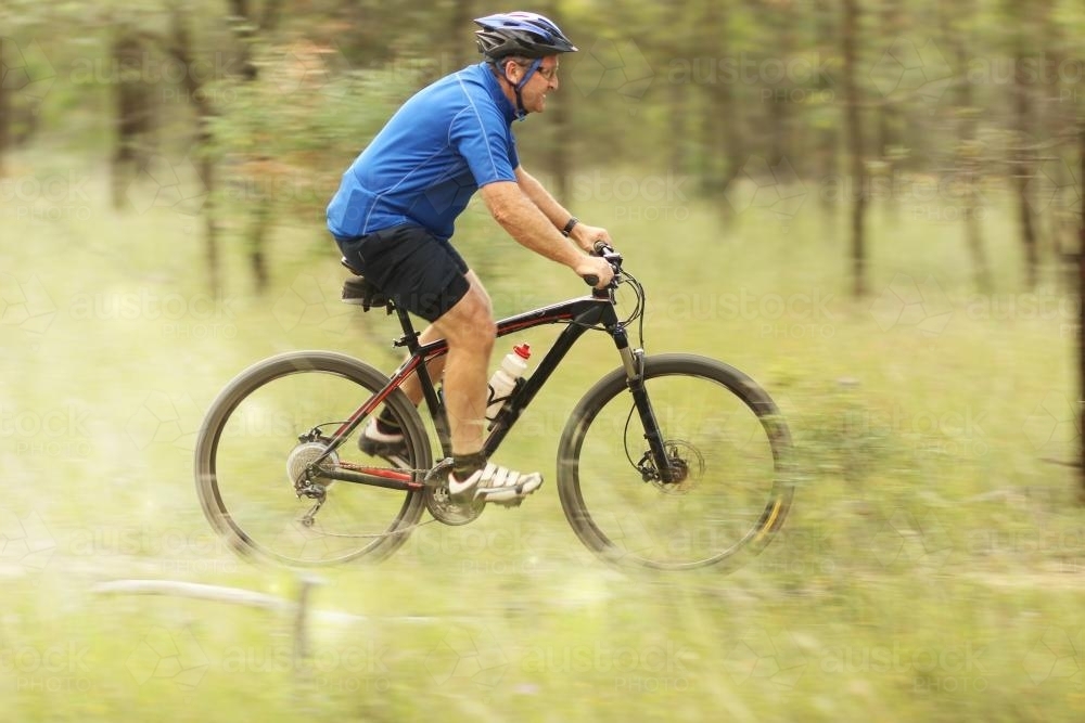 Image of Man riding his pushbike on a dirt track among trees - Austockphoto