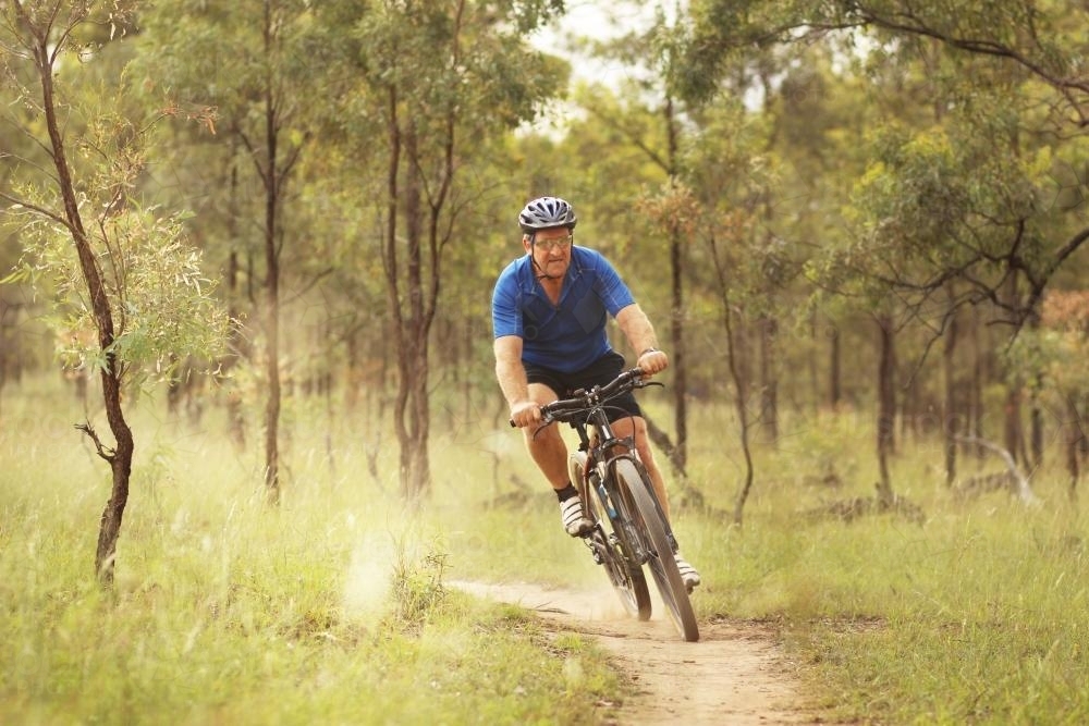 Image of Man riding his pushbike on a dirt track among trees - Austockphoto
