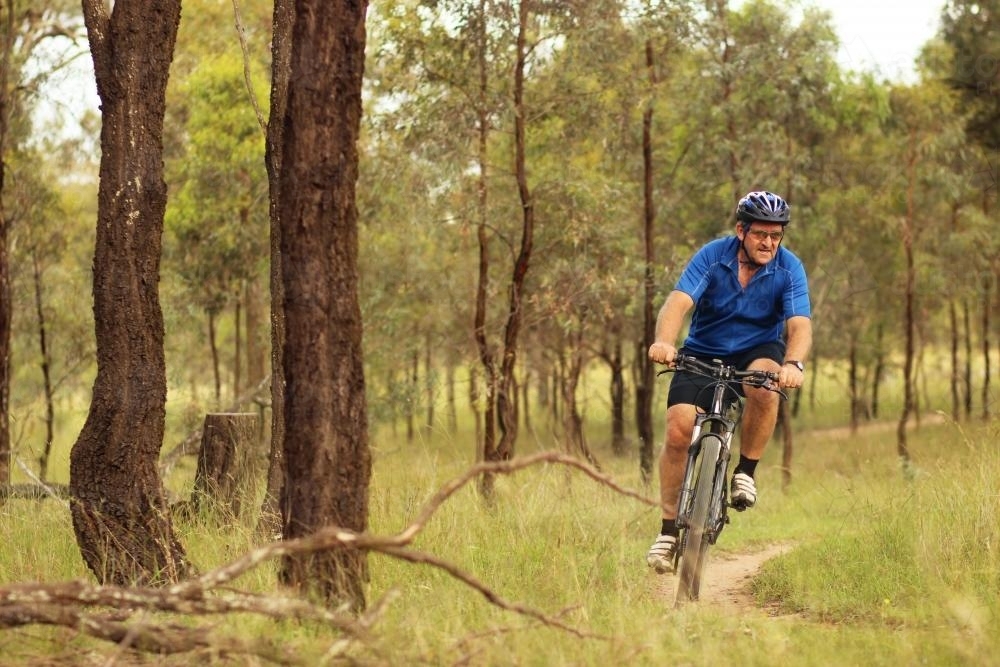 Image of Man riding his pushbike on a dirt track among trees - Austockphoto