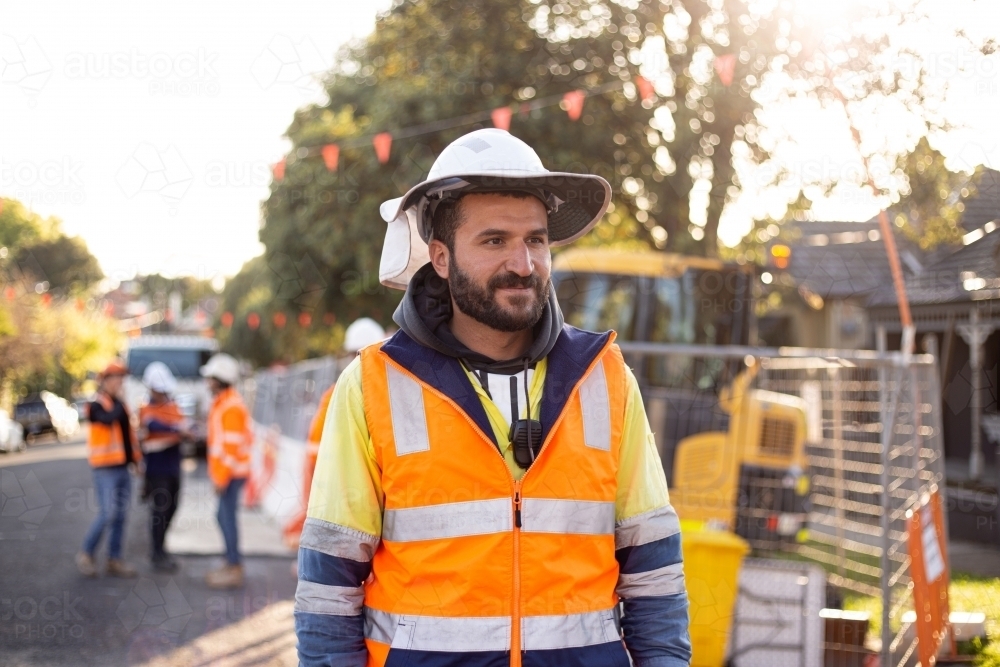Image of man road worker with beard wearing white hat with yellow and orange high-vis jacket ...