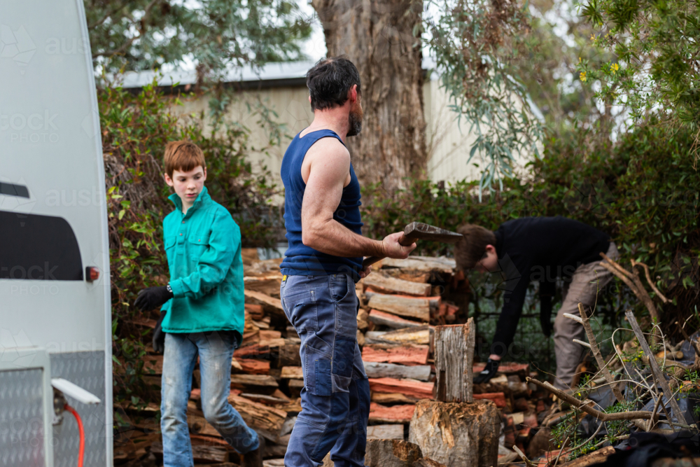Image of Man splitting wood for fire with son helping him stack ...