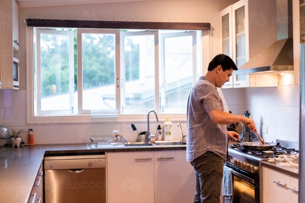 Image of Man standing in the kitchen cooking food in a stovetop pan ...