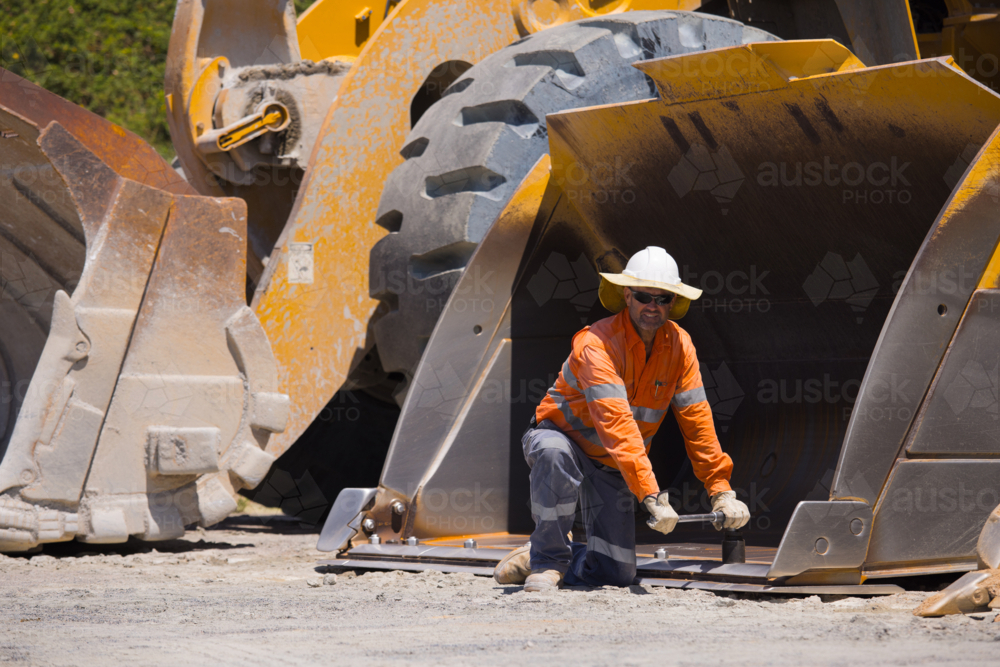 Image of Man tightening the bolts on the bucket of a payloader ...