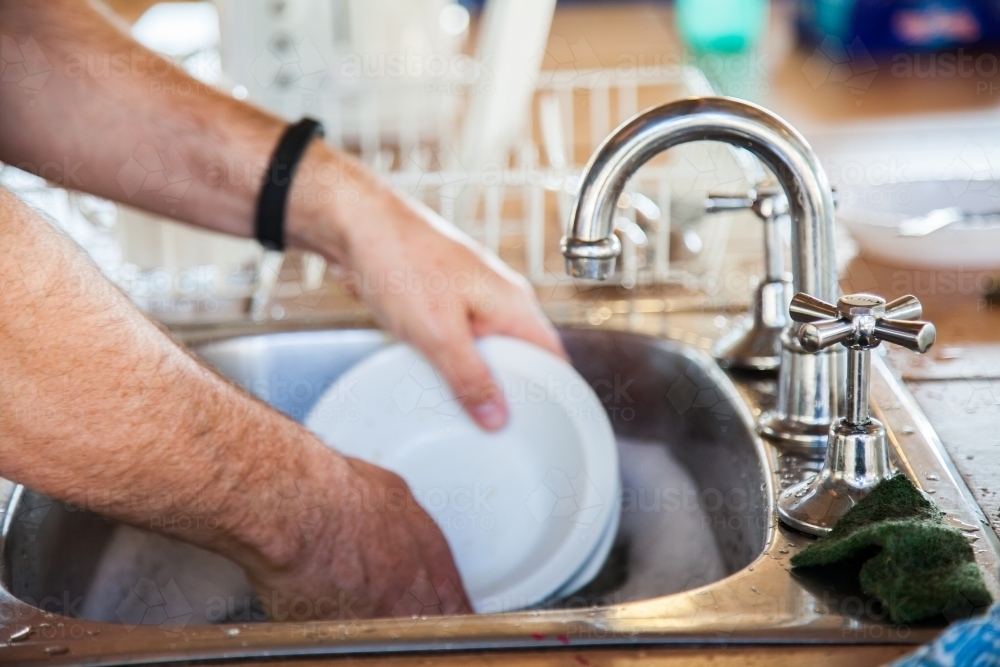 Image of Man washing up plates in sink - Austockphoto