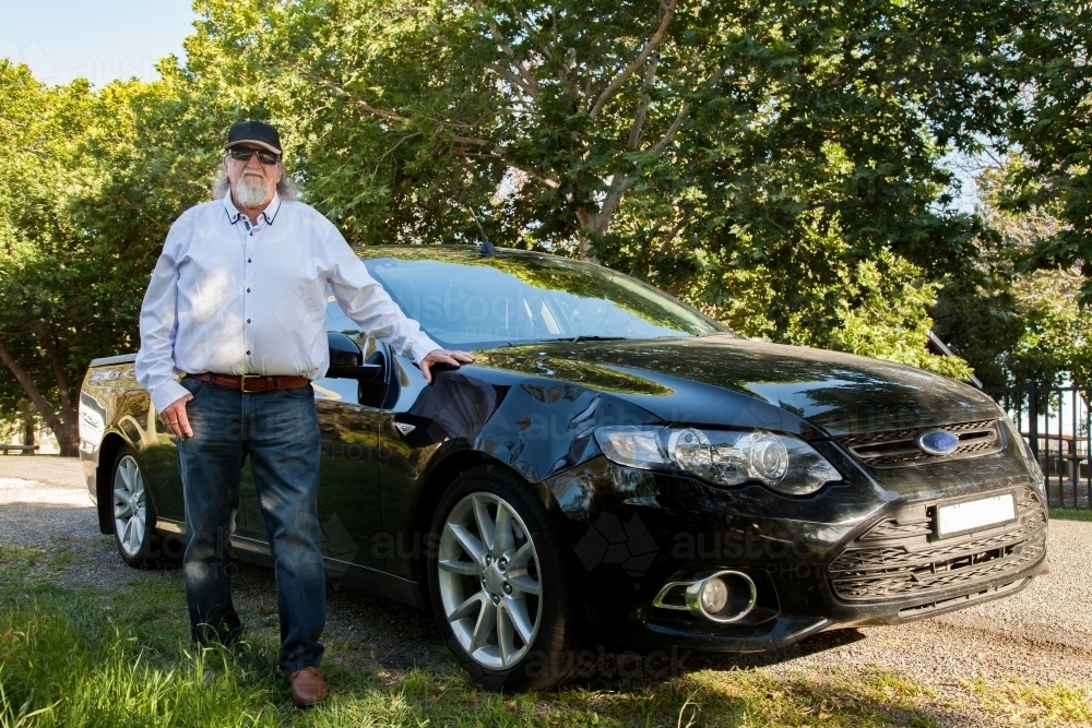 Image of Man with cap standing beside his black ute - Austockphoto