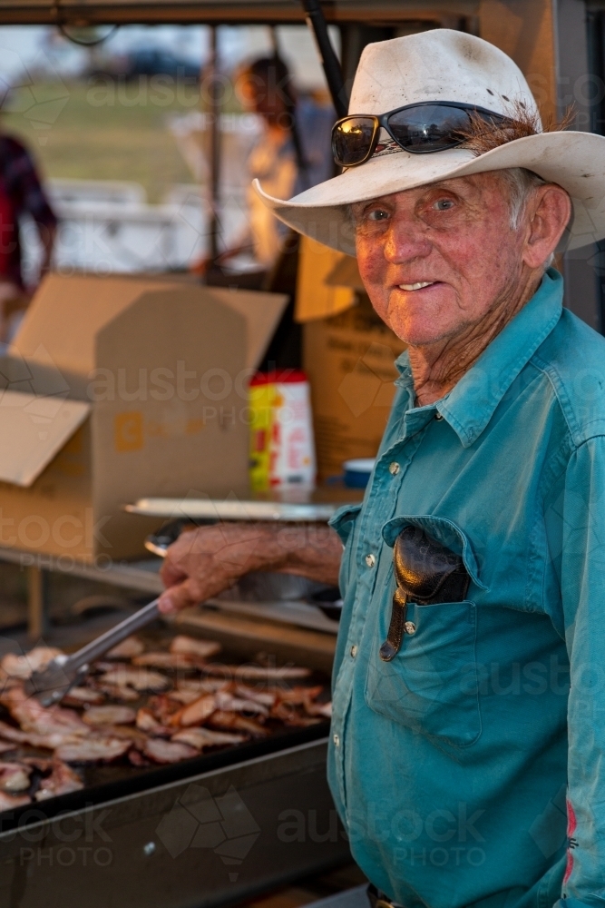 Image of Mature farmer cooking up lots of bacon on a hotplate ...