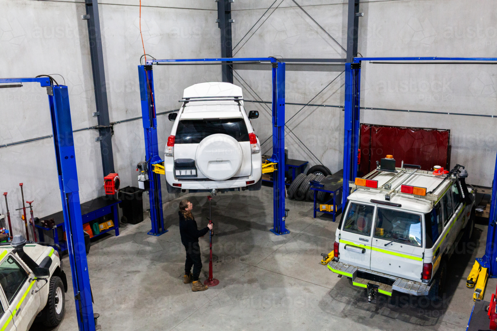 Image of mechanic working on cars on lift in clean workshop - Austockphoto