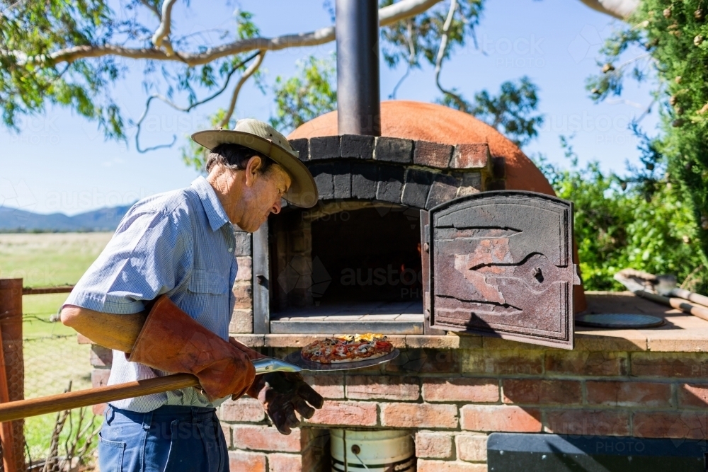Image of Middle aged man cooking homemade pizza in oven outdoors ...