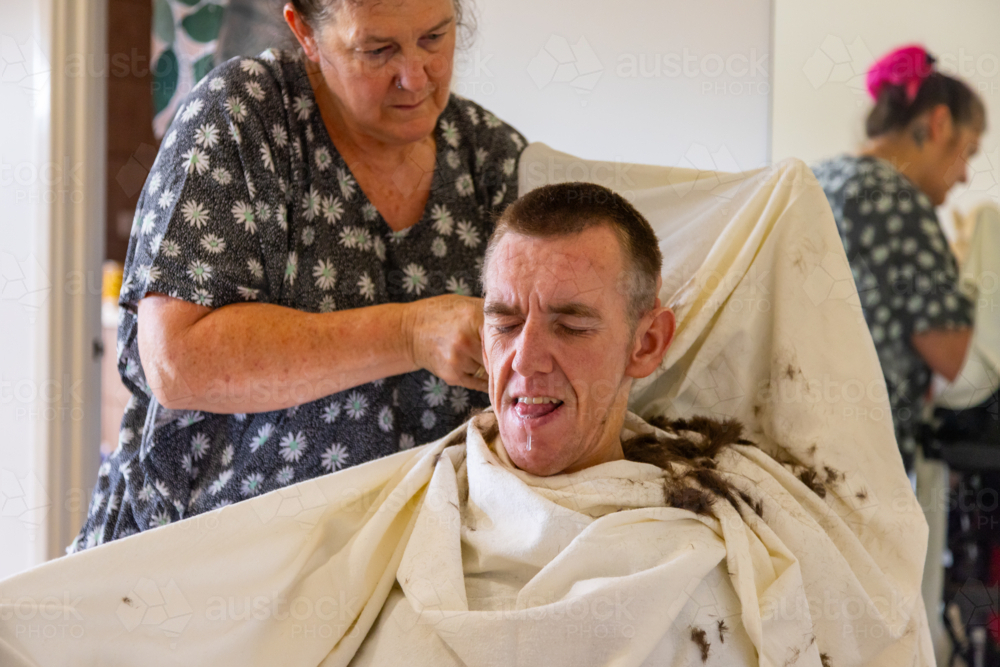 Image of Middle aged woman carer cutting hair on head of young man with ...