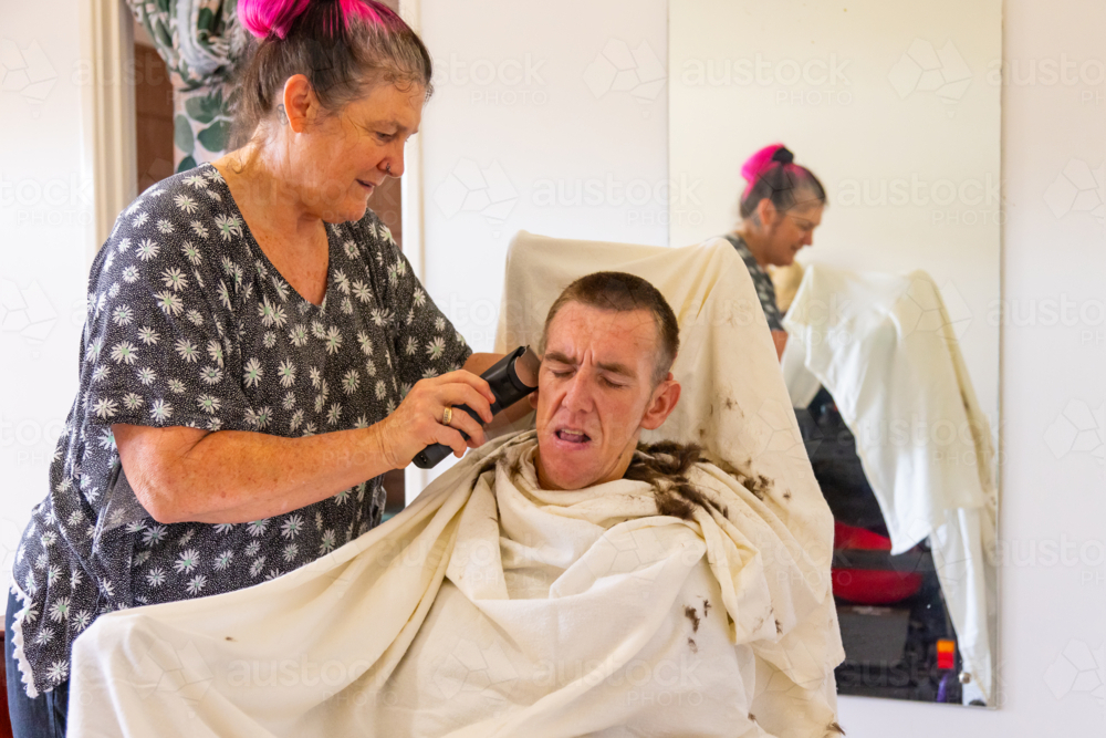Image of Middle aged woman carer cutting hair on head of young man with ...