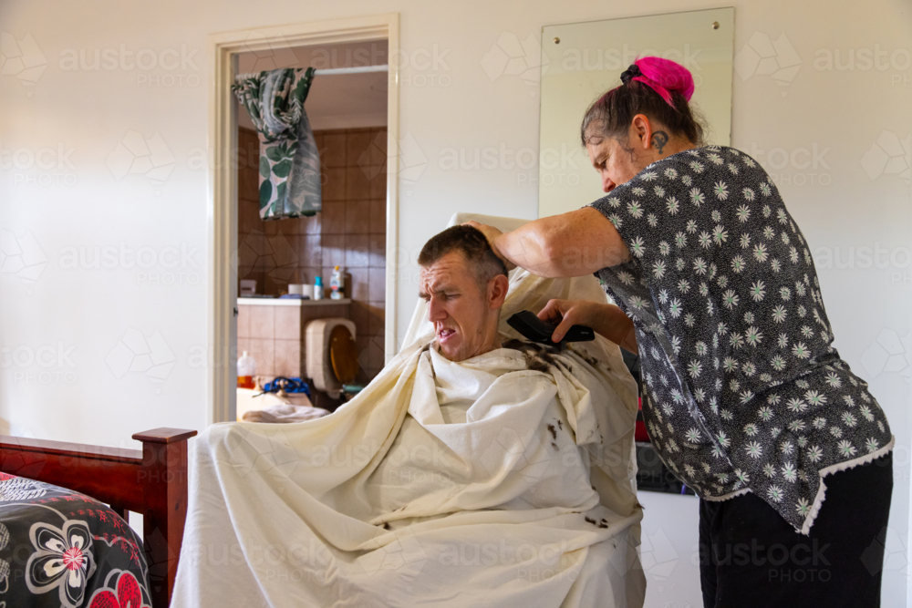 Image of Middle aged woman carer cutting hair on head of young man with ...