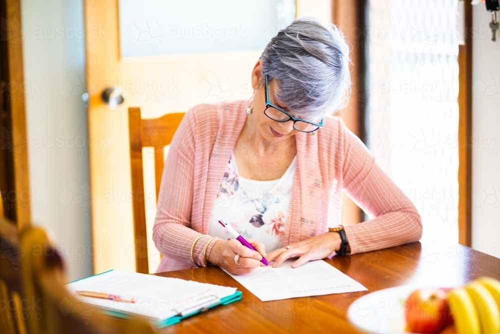 Image of Middle aged woman signing paper documents and forms - Austockphoto