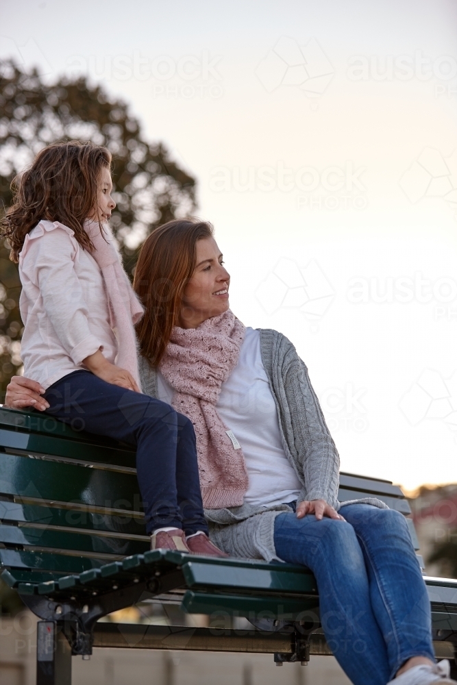 Image of Mother and daughter sitting on park bench at park on sunset ...