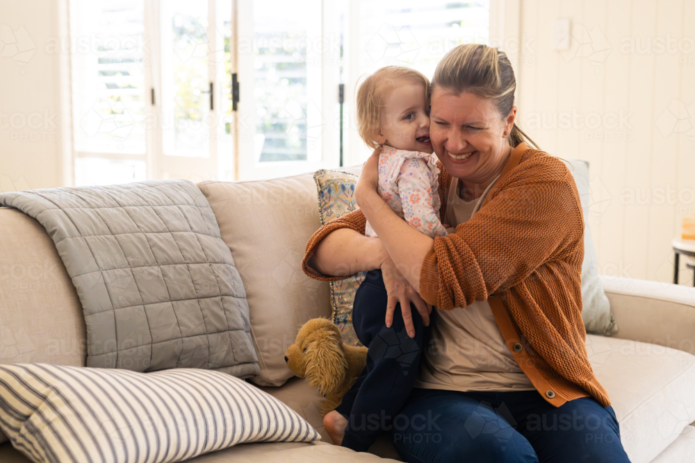 Image of Mother embracing toddler daughter in the couch - Austockphoto