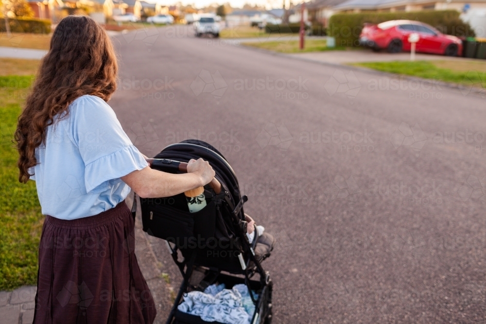 Image of mother pushing pram taking baby for walk down quiet suburban street - Austockphoto