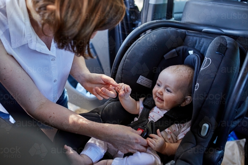 Image of Mother putting baby girl into car seat - Austockphoto
