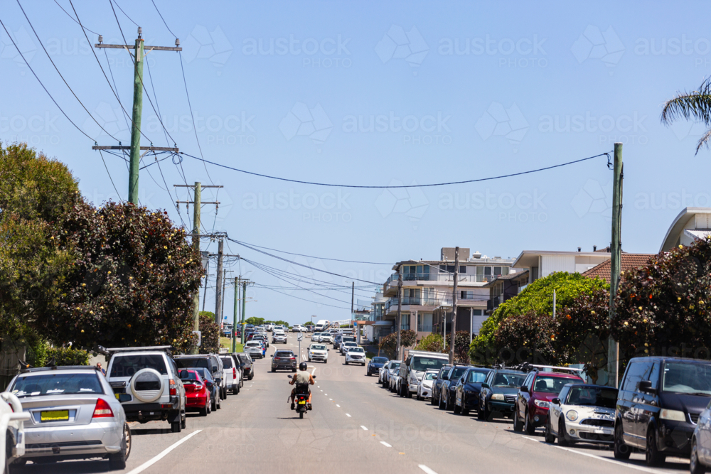 Image of Motorbike travelling down road in coastal city with parked ...