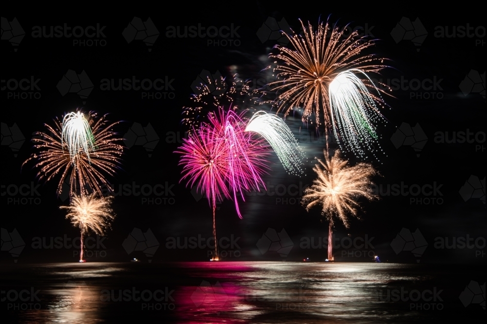 Image of Multi coloured fireworks exploding over an ocean in the night ...